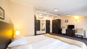 Quarto de hotel com uma cama grande, uma escrivaninha, uma cadeira, uma televisão e um espelho.