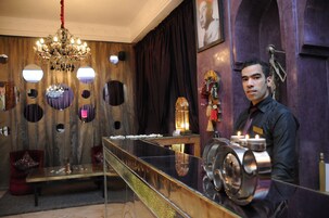 Uma área de bar com um bartender, um candelabro e um espelho com recortes circulares.