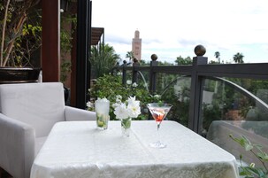 Uma mesa com toalha branca, dois vasos com flores e uma taça de martini com bebida vermelha.
