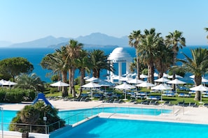 Uma área de piscina com espreguiçadeiras e guarda-sóis, um toboágua e vista para o mar e as montanhas.