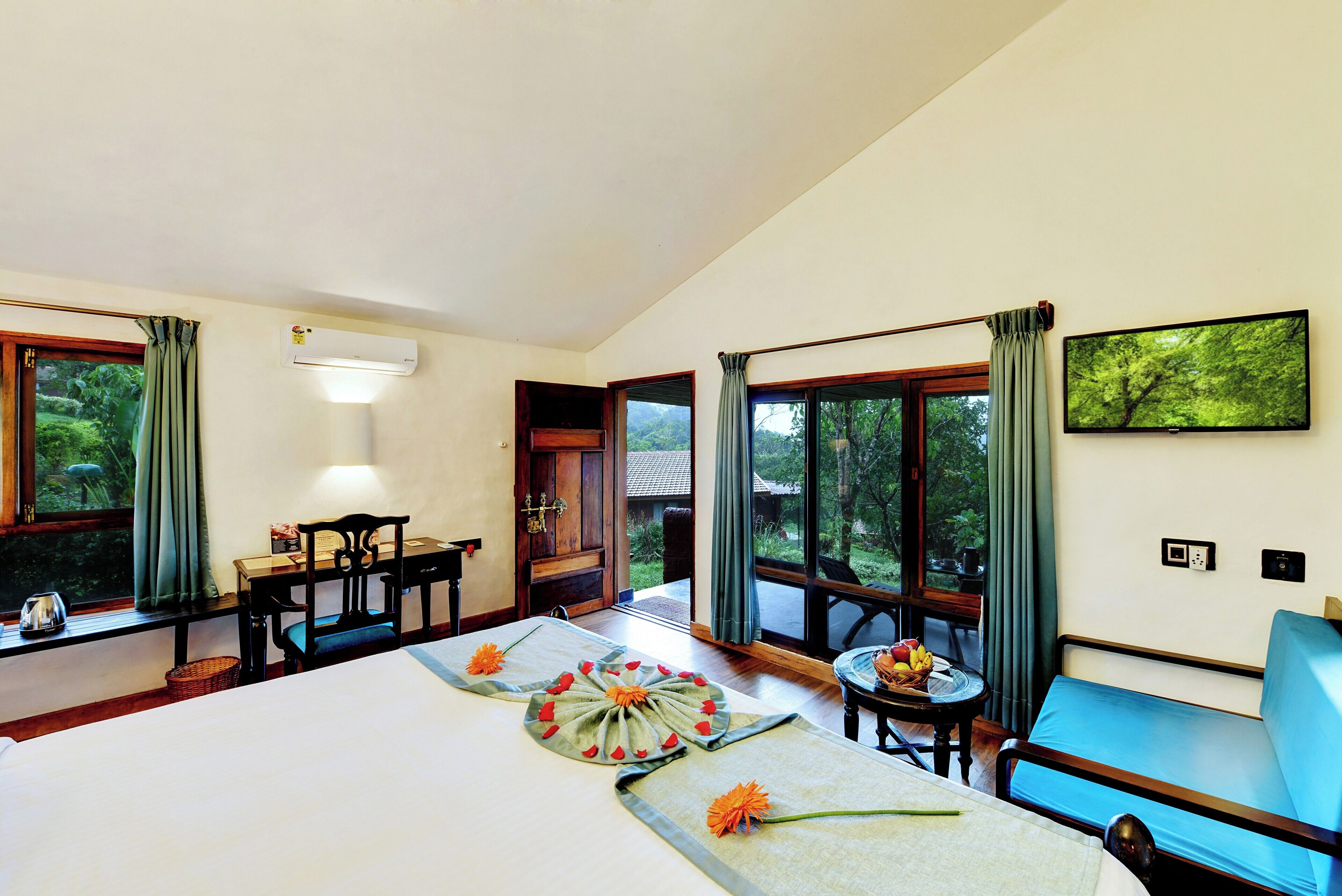 Quarto com cama, escrivaninha, cadeira, mesa com uma fruteira e janela com vista para o verde.