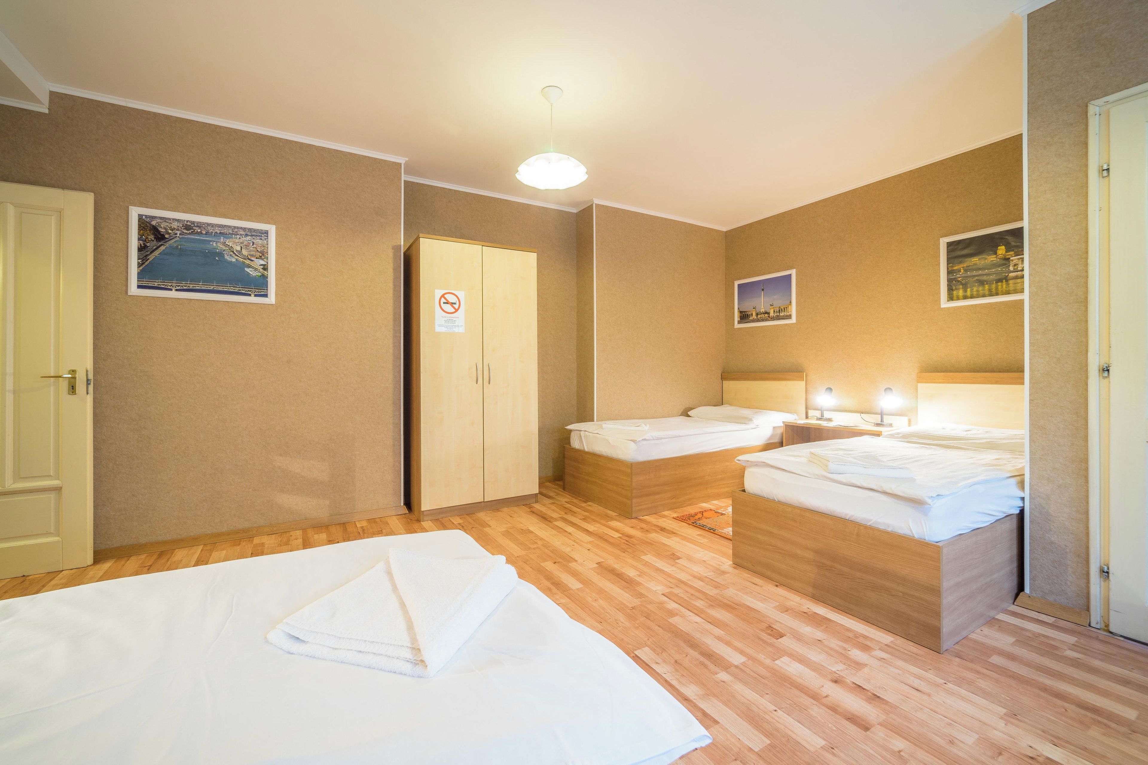 Quarto de hotel com duas camas, um guarda-roupa e duas quadros pendurados na parede.