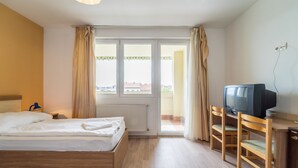 Quarto de hotel com uma cama, uma TV em cima de uma mesa de madeira e vista para o exterior através de uma janela.