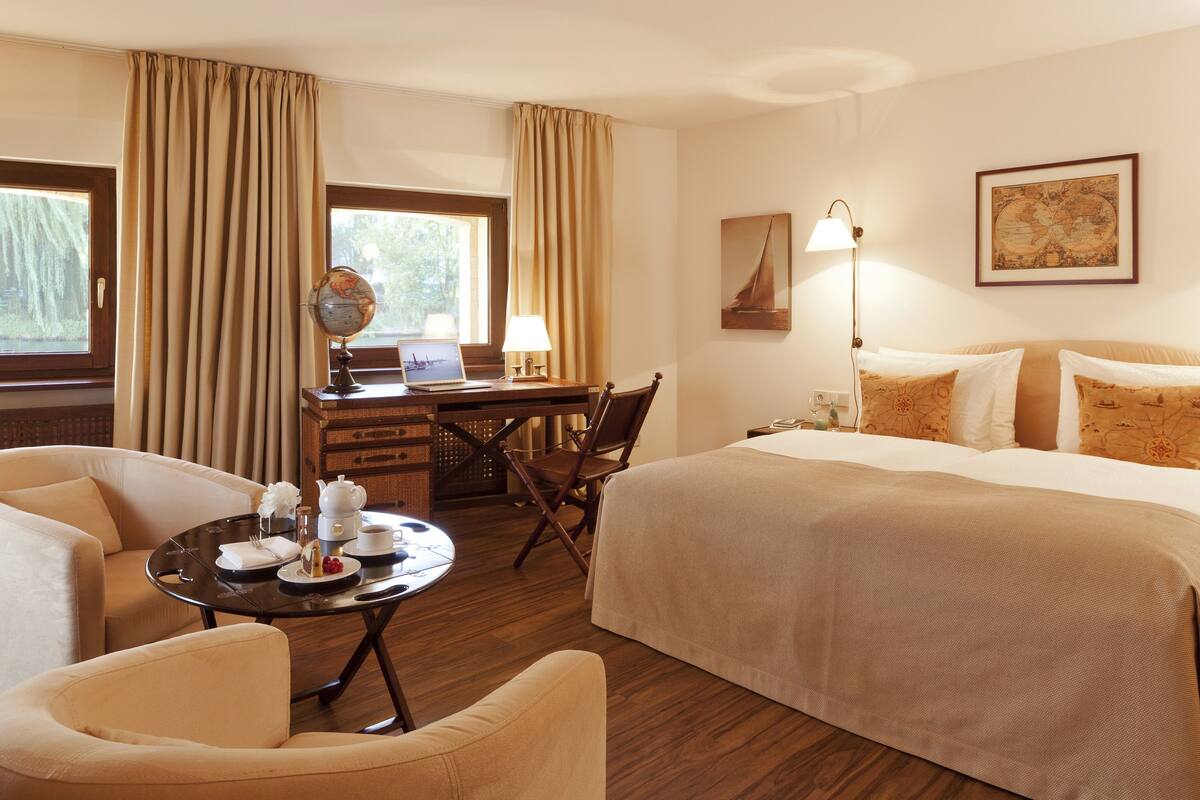 Quarto de hotel com cama, escrivaninha, cadeira e pequena mesa com abajur.