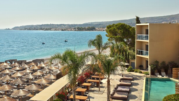Uma área de piscina em resort com espreguiçadeiras, guarda-sóis e vista para o mar.