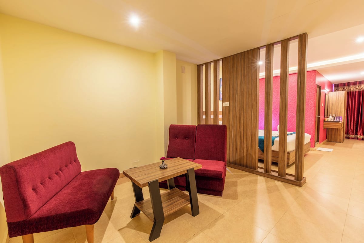 Um quarto com dois sofás vermelhos, uma mesa de madeira e um separador com ripas verticais.