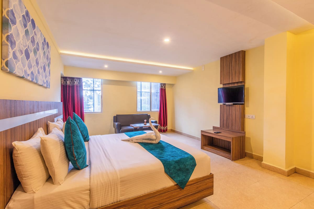 Quarto de hotel com cama, escrivaninha, televisão e janela com cortinas.