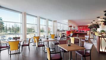 Um restaurante espaçoso com grandes janelas, móveis modernos e uma parede de destaque vermelha.