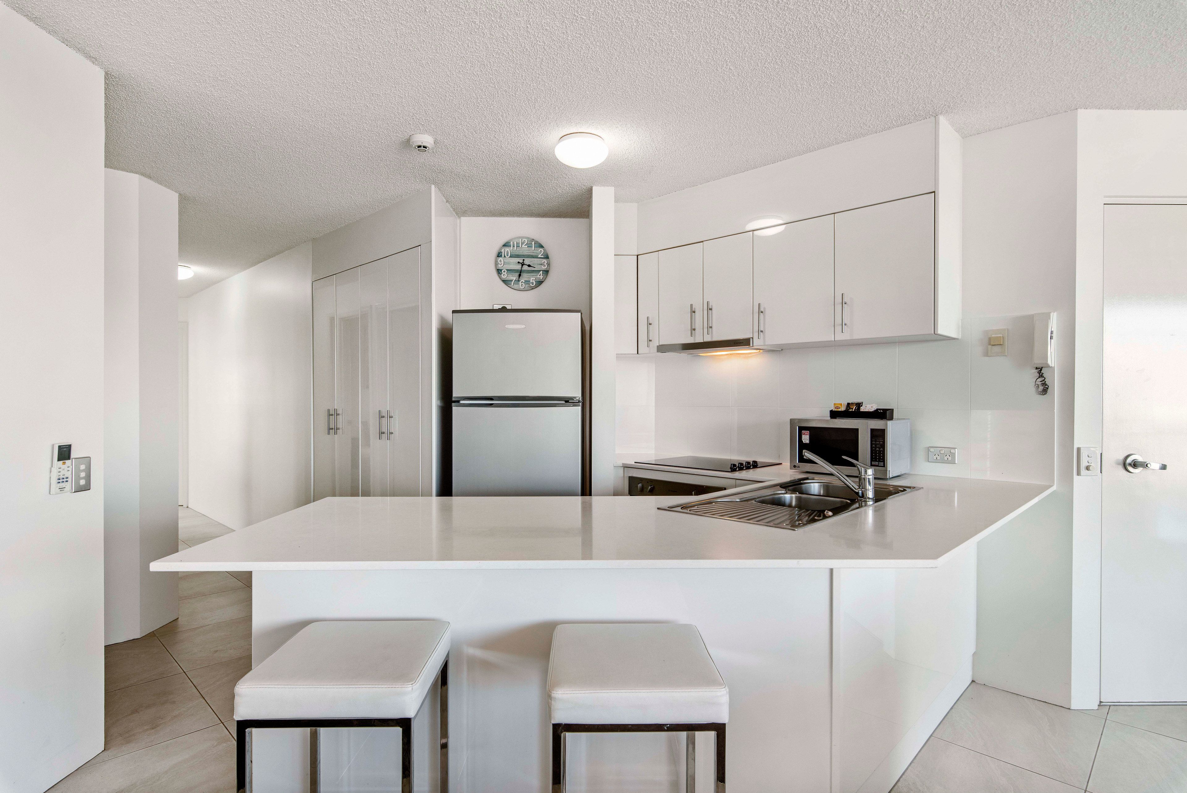 Cozinha moderna com armários brancos, uma ilha central com banquetas, micro-ondas e frigorífico.