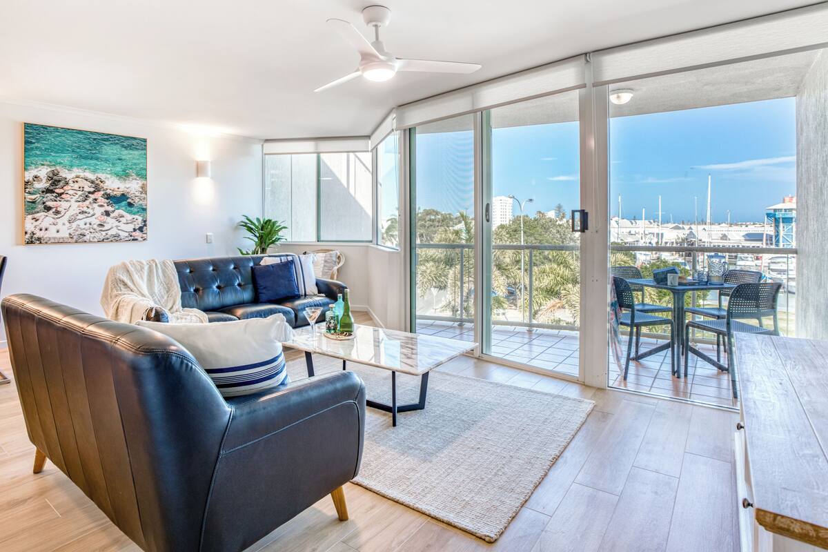 Uma sala de estar moderna com um sofá de couro, uma mesa de centro e vista para a marina através de grandes janelas.
