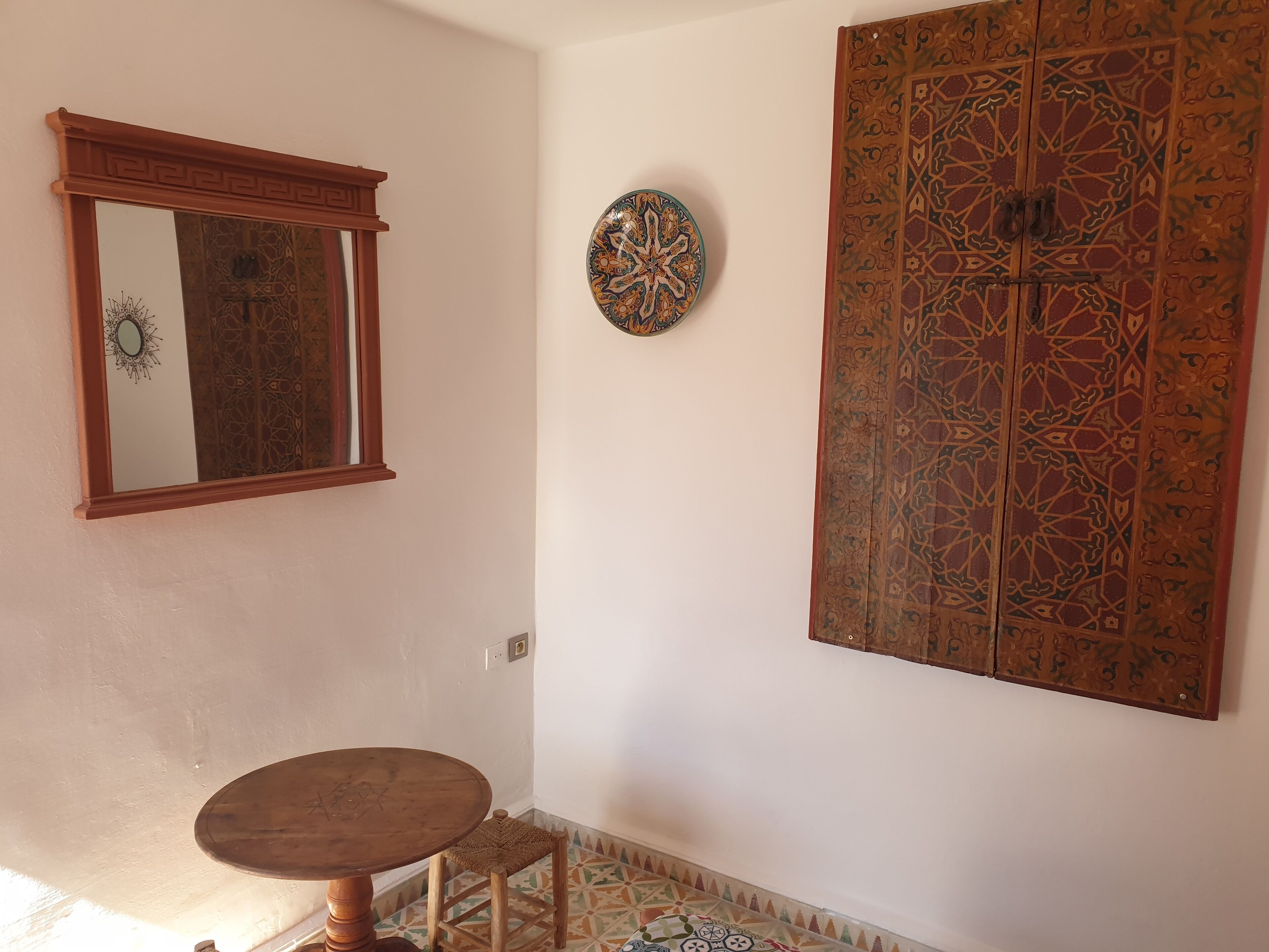 Um quarto com uma mesa de madeira, um espelho, um prato decorativo e uma porta grande com padrão.