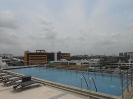 Piscina no terraço com espreguiçadeiras e vista para a paisagem urbana.