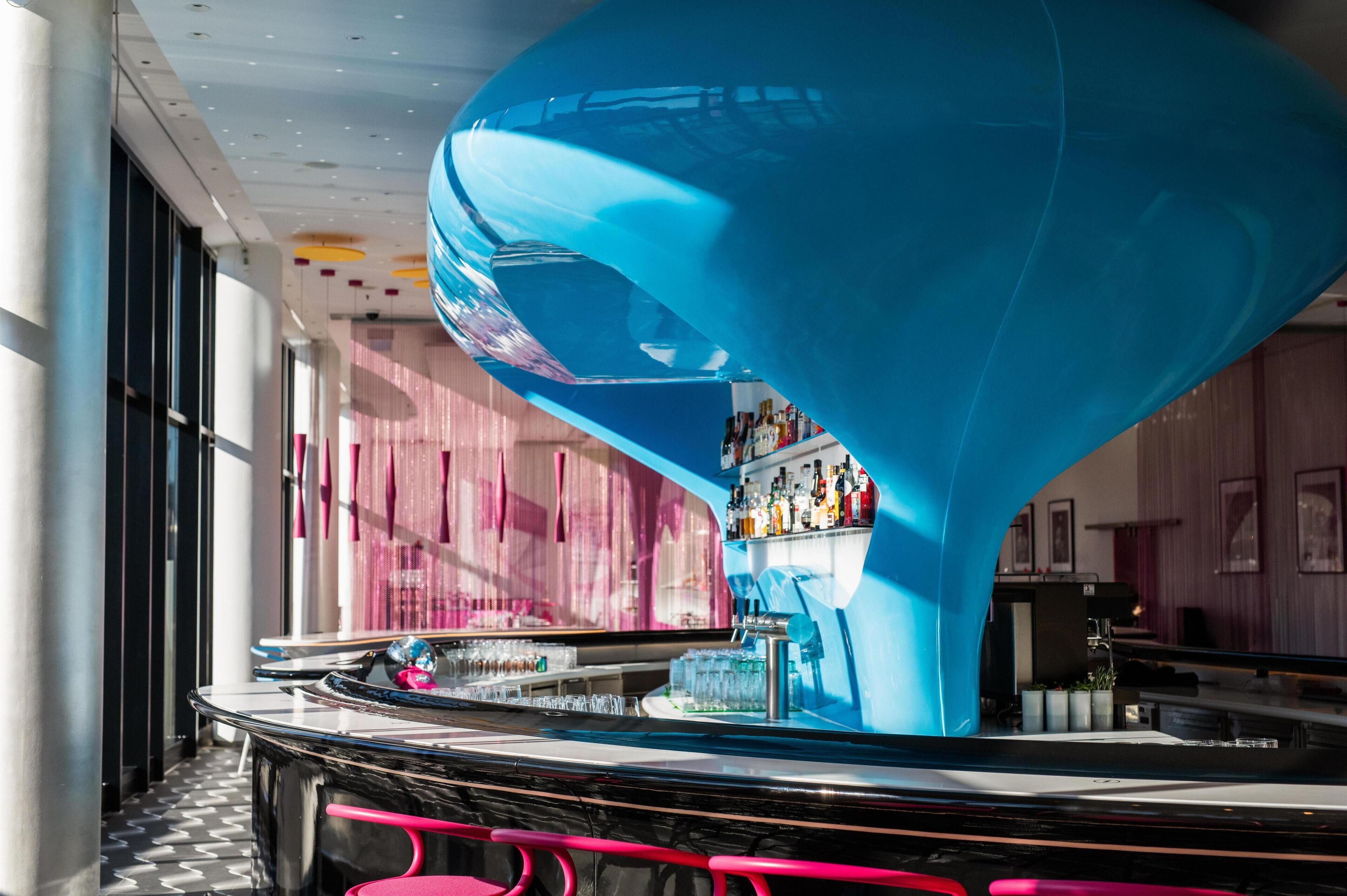 Uma área de bar moderna com estrutura azul marcante, balcão e espaço de estar com cadeiras cor-de-rosa.