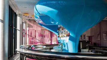 Uma área de bar moderna com estrutura azul marcante, balcão e espaço de estar com cadeiras cor-de-rosa.