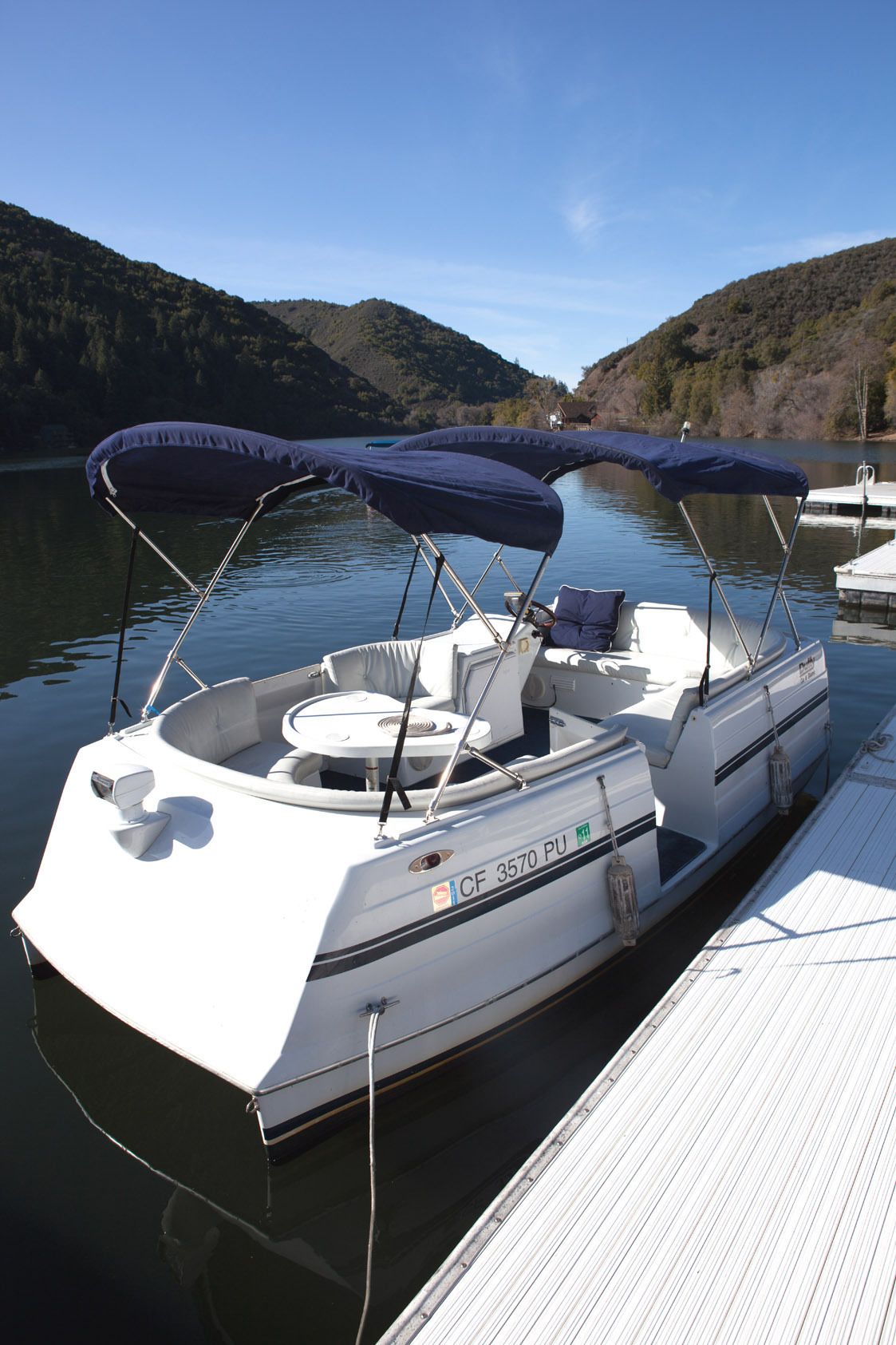 Um barco a motor branco atracado num cais, com área de estar coberta e uma pequena mesa.