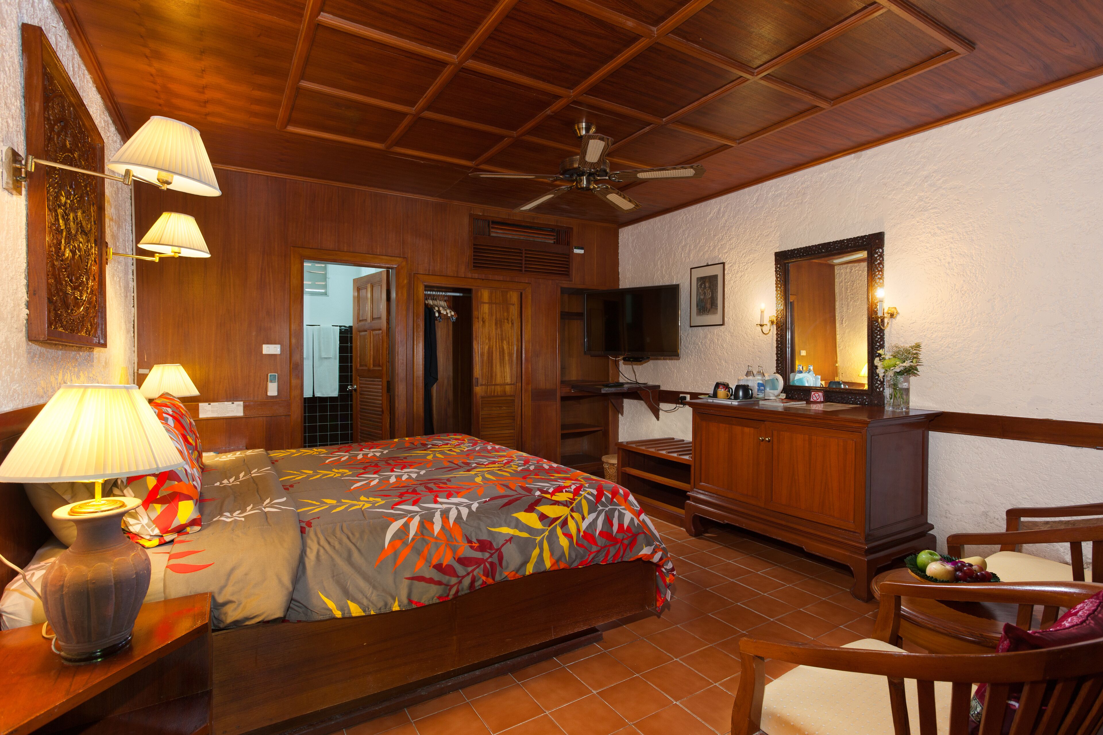 Quarto de hotel com cama, escrivaninha, cadeira, televisão e ventoinha no teto.