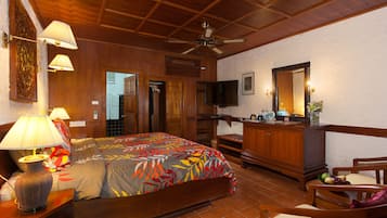 Quarto de hotel com cama, escrivaninha, cadeira, televisão e ventoinha no teto.