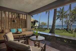 Varanda com vista para o mar, sofá com almofadas, mesa com uma planta e cerca de bambu.