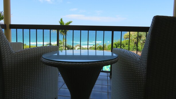 Varanda com vista para o oceano, mesa redonda e cadeiras de vime.