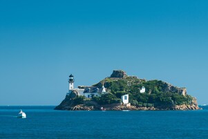 Uma ilha costeira com um farol, vários edifícios e um pequeno barco na água.