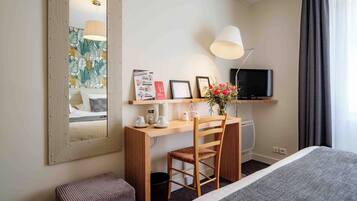 Quarto de hotel com cama, escrivaninha, cadeira, televisão, espelho e janela com cortinas.