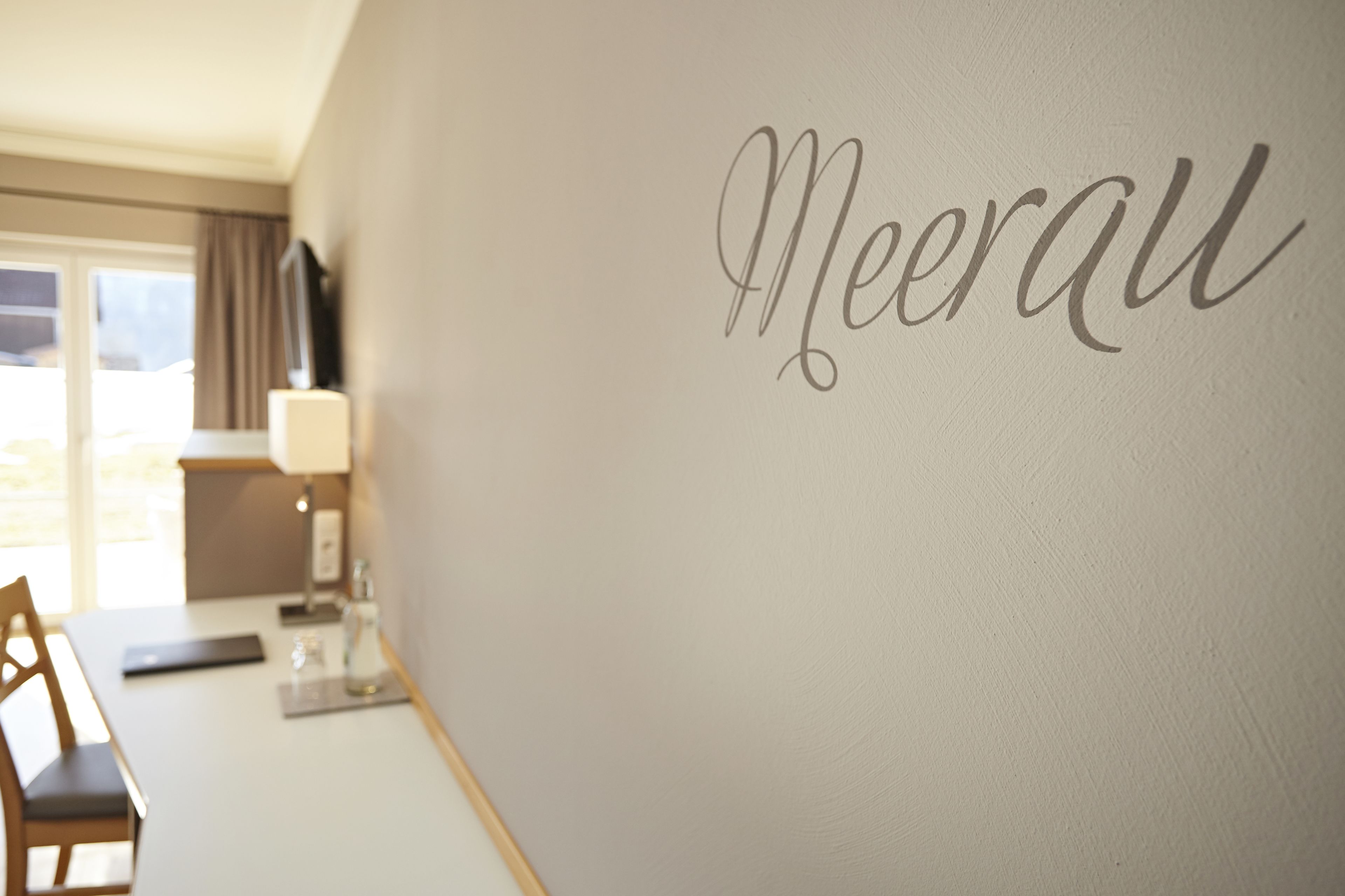 Quarto de hotel com design minimalista, com uma cama, uma mesa e uma cadeira. O quarto possui uma janela grande que oferece vista para o exterior.