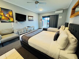 Quarto de hotel com uma cama grande, um sofá, uma escrivaninha com cadeiras, uma TV de tela plana e obras de arte nas paredes.