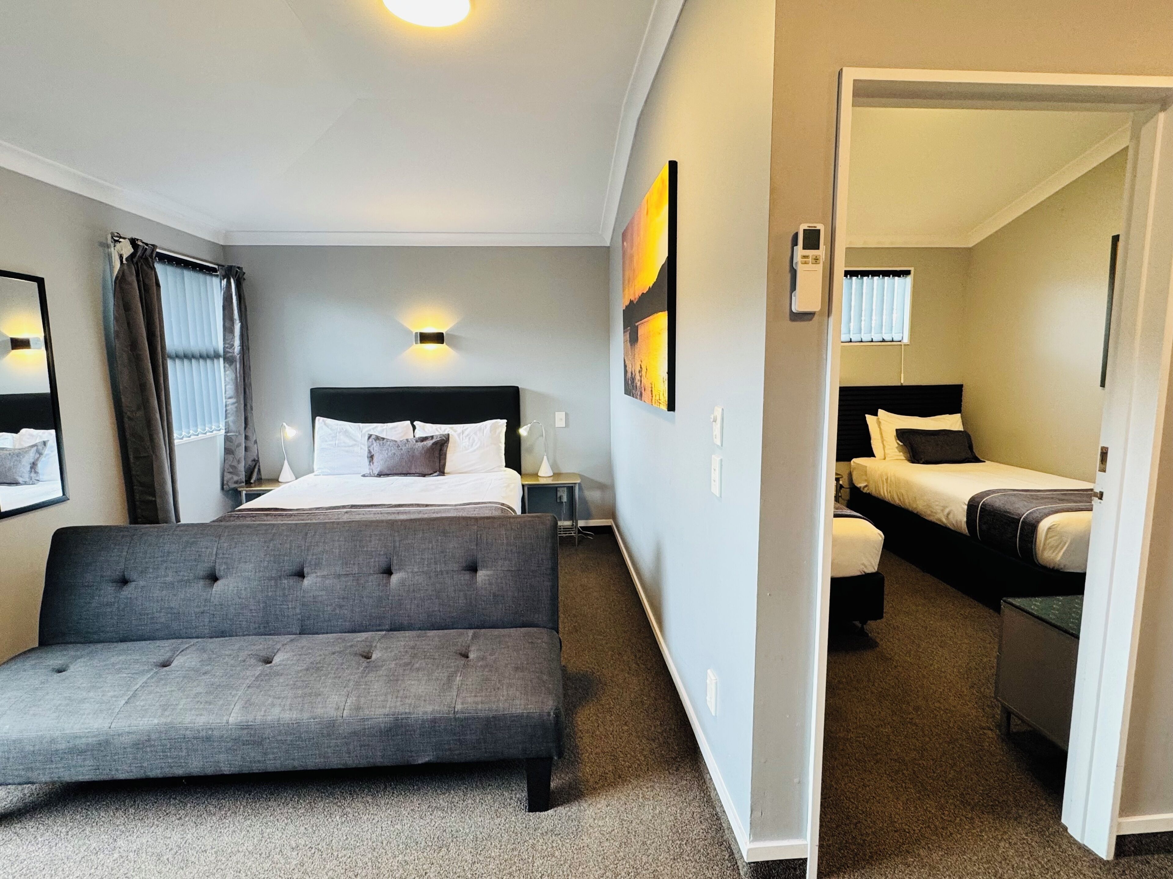 Quarto de hotel com uma cama grande, uma cama menor, um sofá, uma escrivaninha e uma mesa de cabeceira.