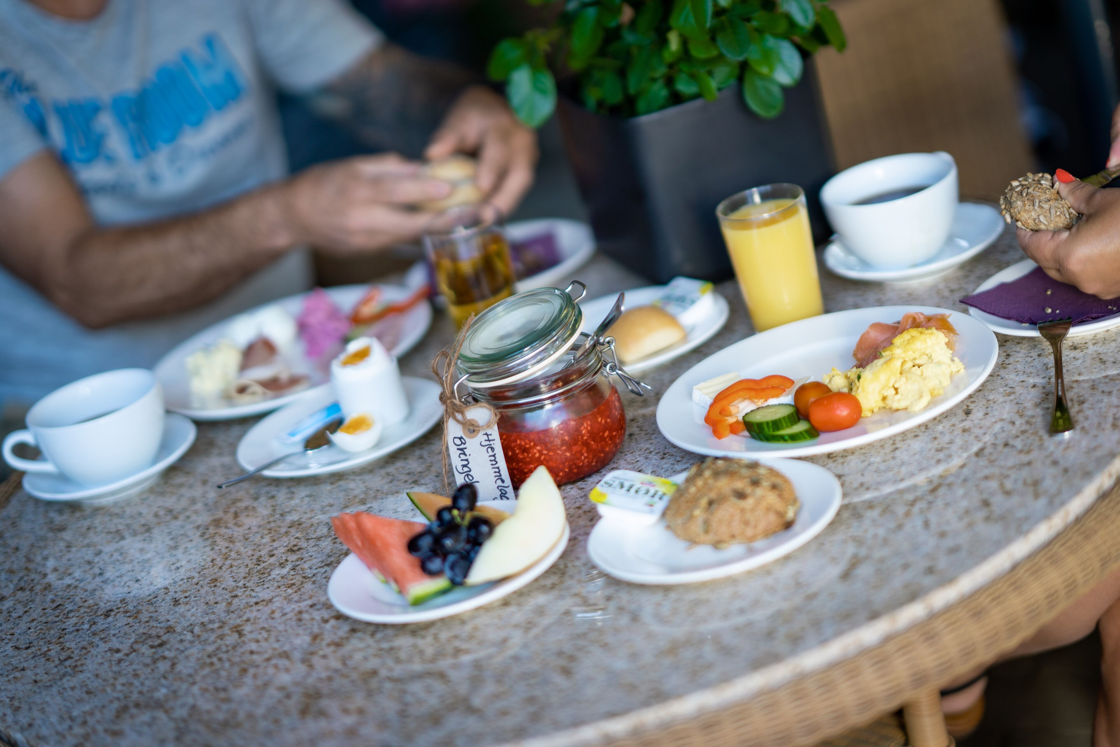 Mesa redonda com itens de café da manhã, incluindo torradas, ovos e frutas.