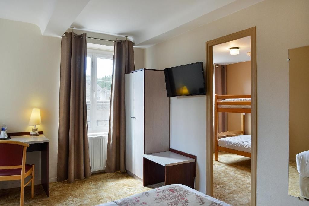 Quarto de hotel com cama, escrivaninha com cadeira, televisão na parede e beliche.