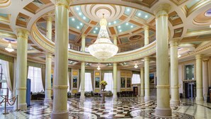 Um saguão imponente com tetos altos, grandes lustres e piso de mármore quadriculado.