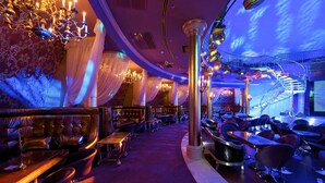 Um interior luxuoso com lustres ornamentados, assentos macios e uma escadaria imponente.