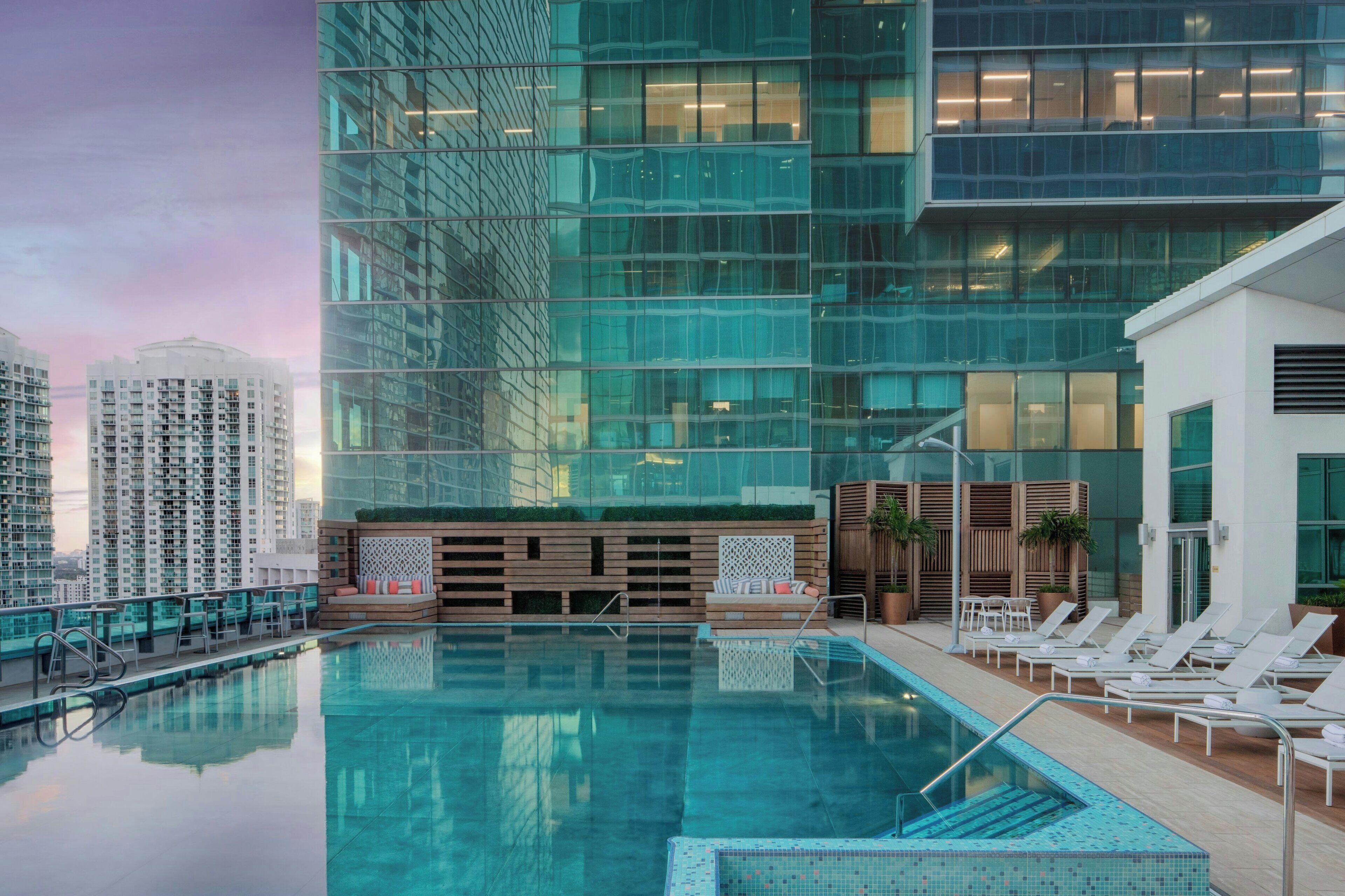 Um hotel moderno com piscina infinita no terraço, cadeiras de lounge e vista para edifícios altos.