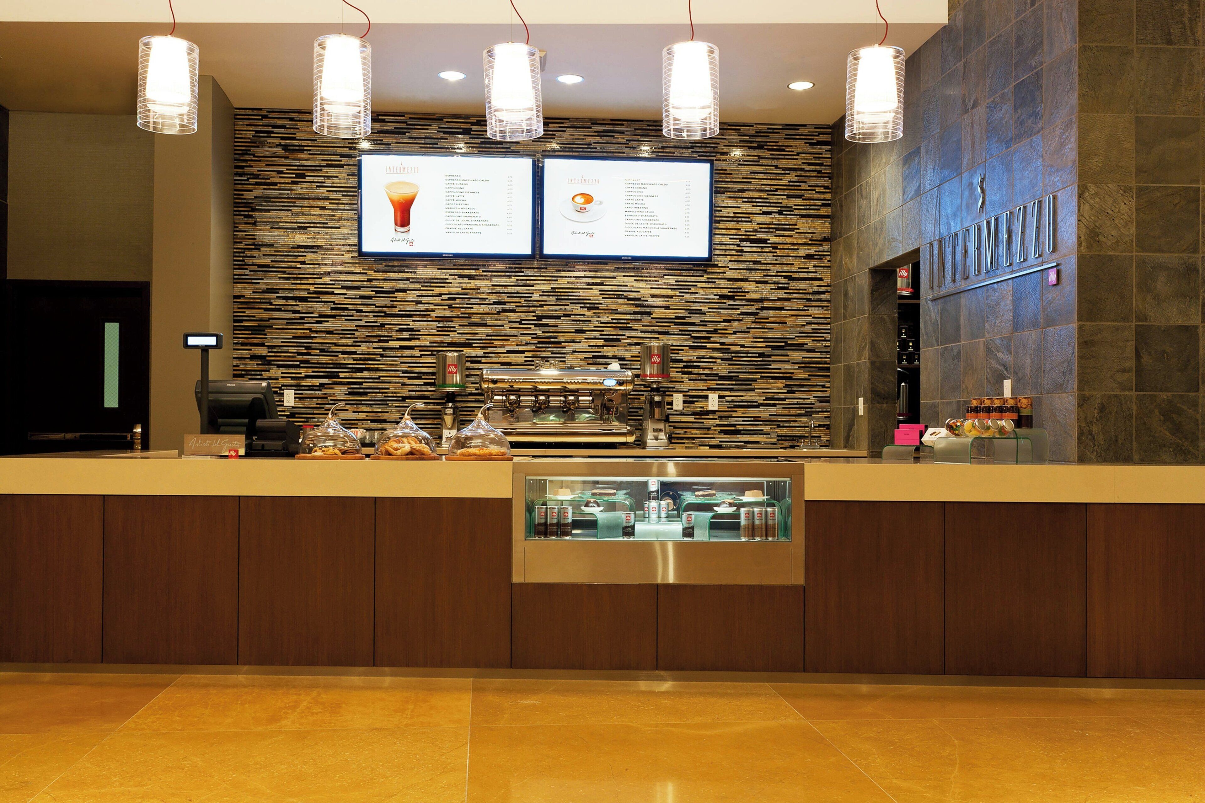 Um hall de hotel moderno com parede de pedra, um painel digital de menu, uma máquina de café e uma vitrine de vidro.