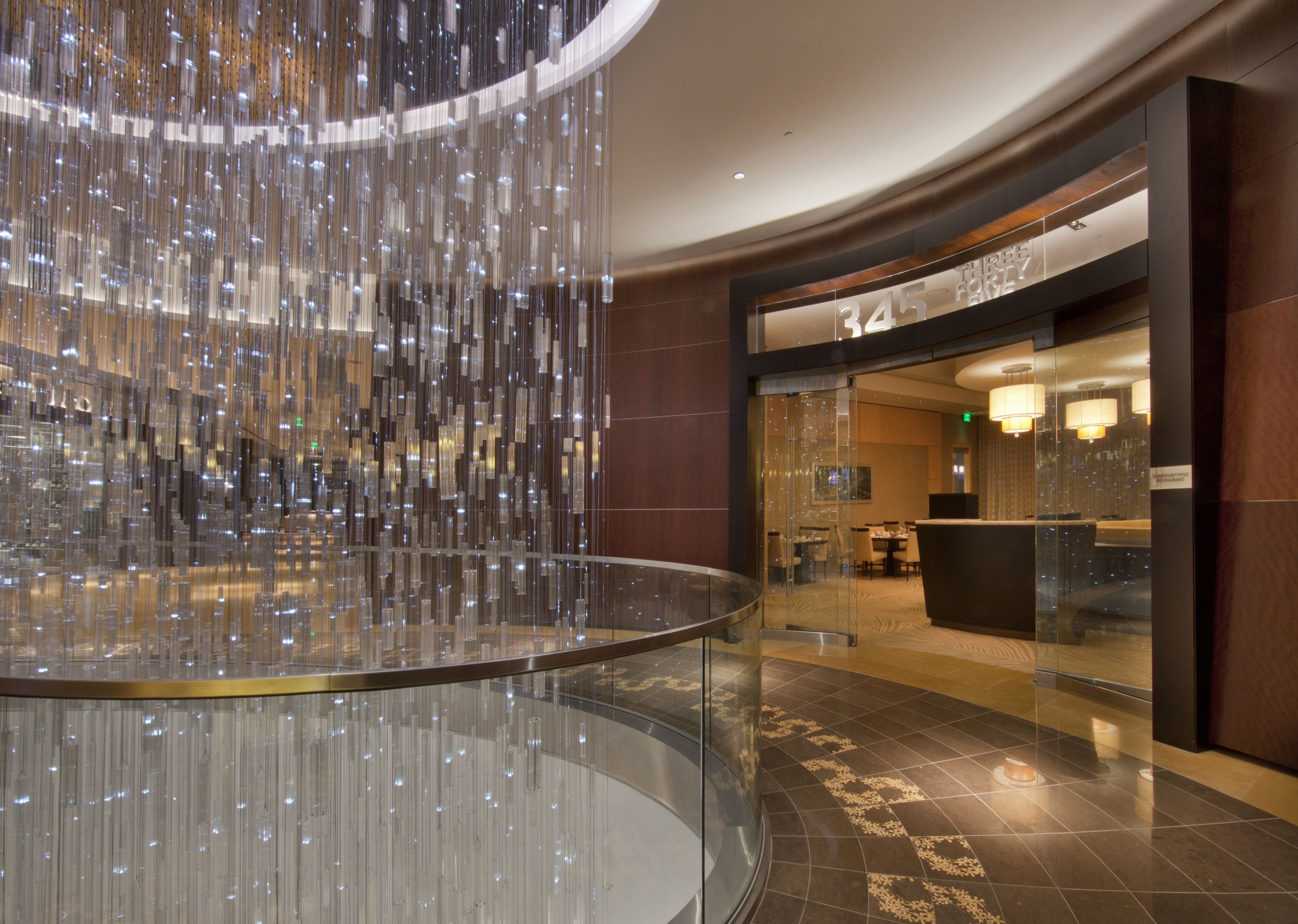 Um lobby moderno com guarda-corpo de vidro, luminária pendente e balcão de recepção.