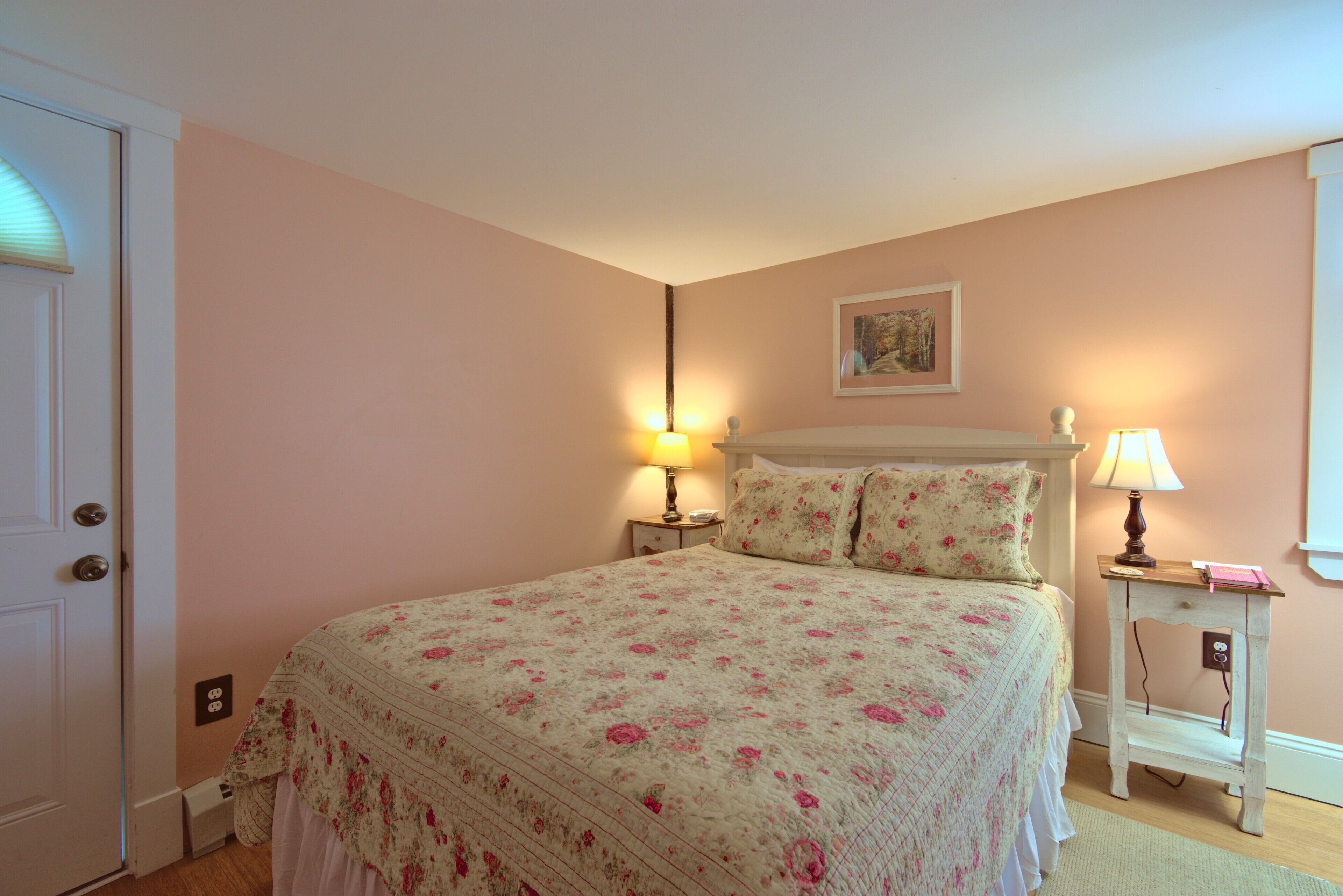 Um quarto com colcha florida, duas luminárias de cabeceira, mesa de cabeceira e uma porta.