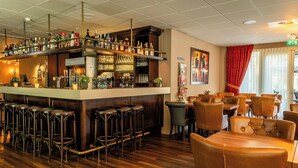 Uma área de bar com banquetas, um balcão com garrafas, copos e uma máquina de café. Há mesas e cadeiras para refeições.