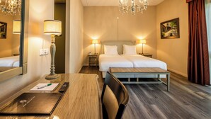 Quarto de hotel com cama, mesas de cabeceira, escrivaninha com cadeira, espelho e lustre.