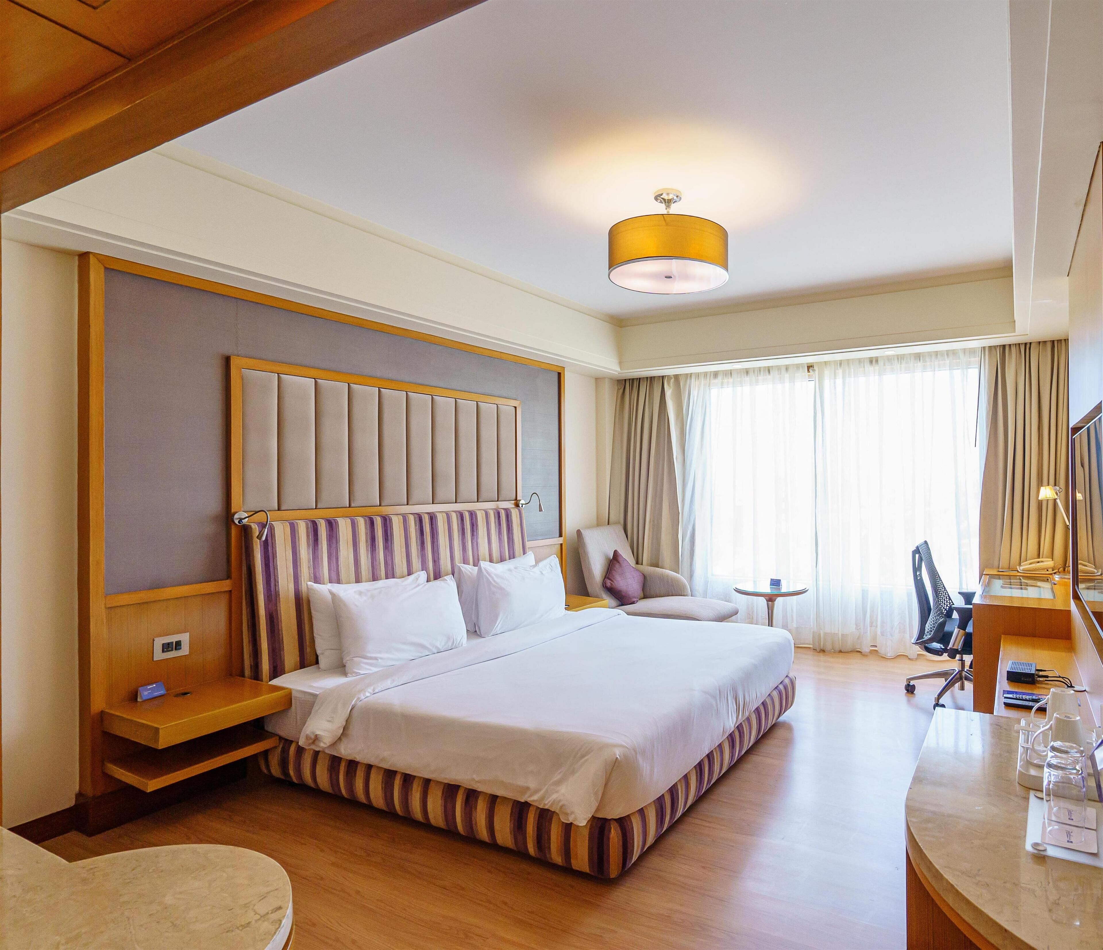 Quarto de hotel com uma cama grande, uma mesa, uma cadeira e um abajur.