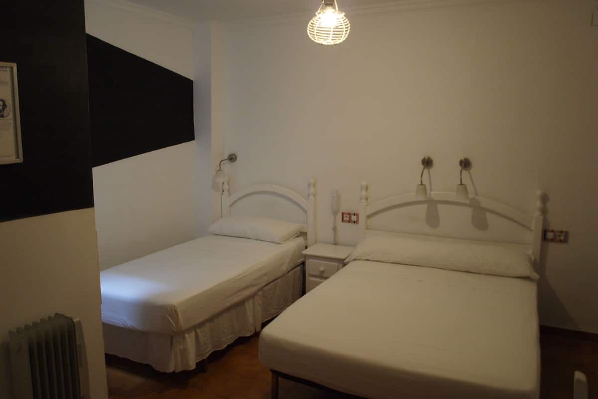 Quarto com duas camas de solteiro, mesa de cabeceira com abajur e radiador.