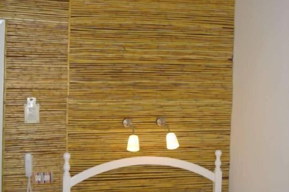 Quarto com parede de ripas de madeira, estrutura de cama branca e duas luminárias de cabeceira.