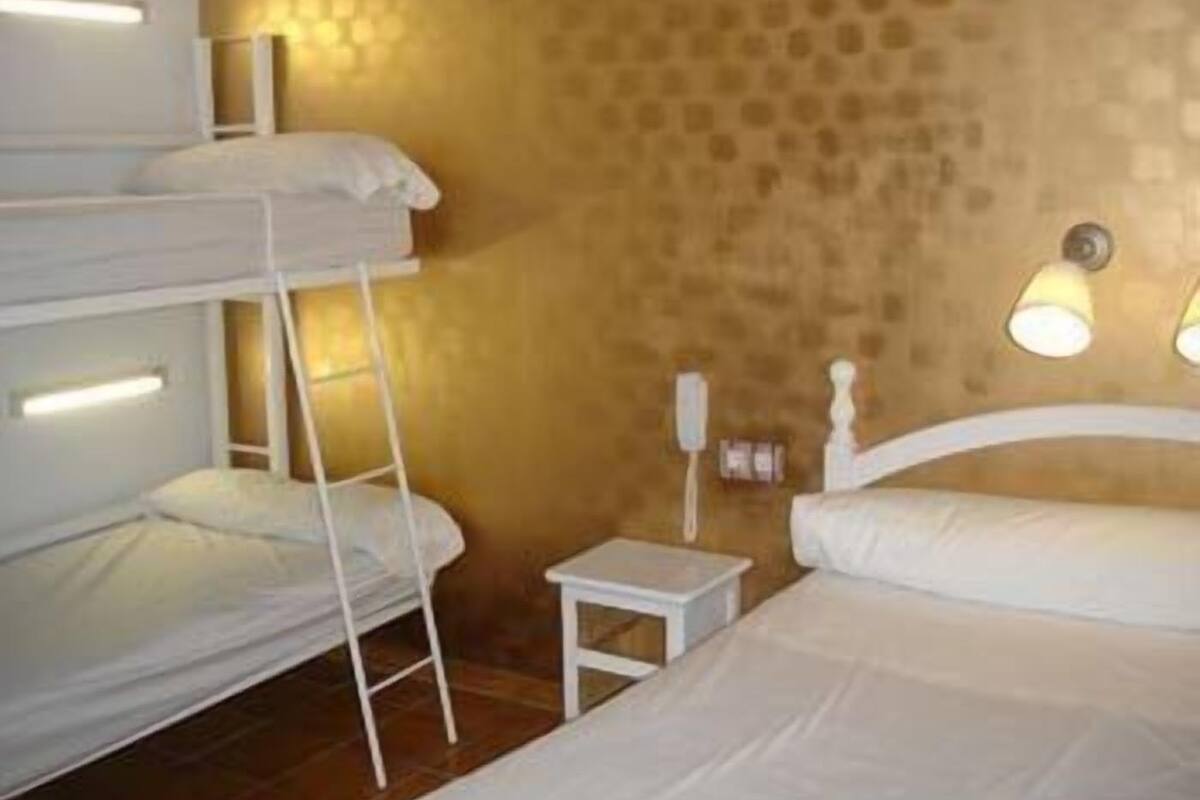 Quarto com beliches, uma pequena mesa de cabeceira e uma luminária fixada na parede.