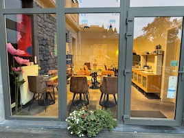 Restaurante com fachada de pedra, mesas internas e vista para a paisagem urbana através de grandes janelas.