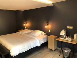 Quarto de hotel moderno com uma cama grande, mesas de cabeceira, uma cafeteira e uma lixeira.