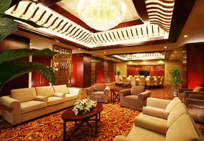 Um saguão de hotel com sofás, poltronas, balcão de recepção e um candelabro.