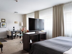 Quarto de hotel com cama, televisão de tela plana em um suporte, escrivaninha com cadeiras e área de jantar.