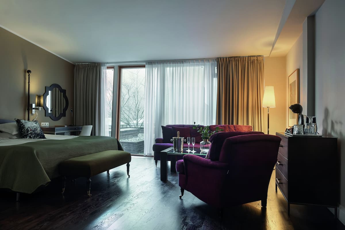 Quarto de hotel com cama, escrivaninha, cadeira, sofá e vista para o exterior.
