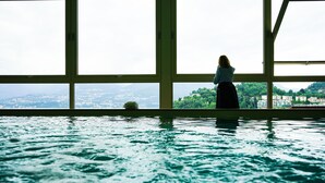 Uma piscina interior ampla com vista para a cidade através de grandes janelas.