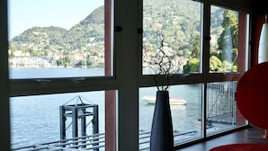 Quarto com grandes janelas dando vista para um lago e colinas, um vaso alto com galhos e um tapete vermelho.