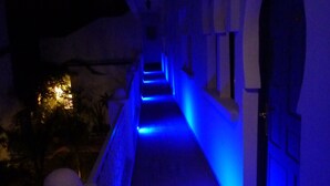 Um corredor com iluminação azul, paredes brancas e portas em arco.
